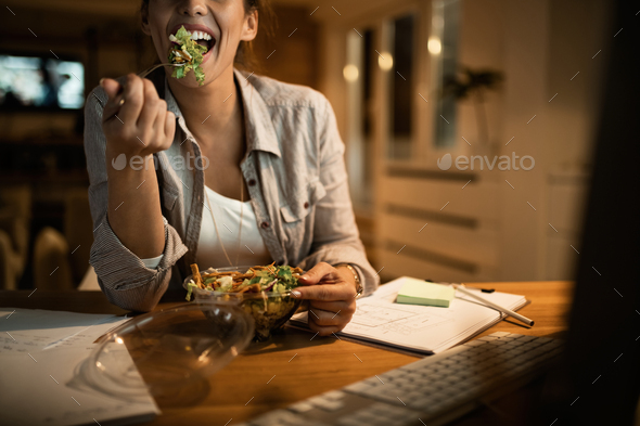 Hungry woman eating salad while working late on a computer. Stock Photo ...