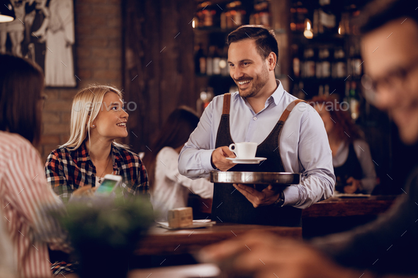 Happy waiter communicating with customers while serving them coffee in ...