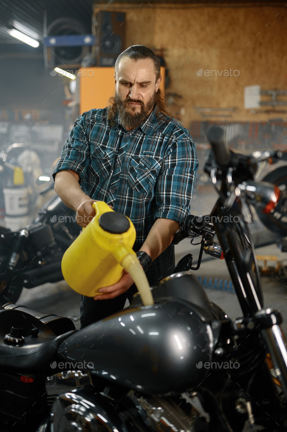 Man biker refueling motorcycle in garage after service repair work ...