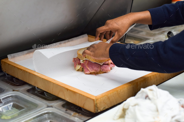 Hands of female diner employee wrapping deli meat sandwich for takeout ...