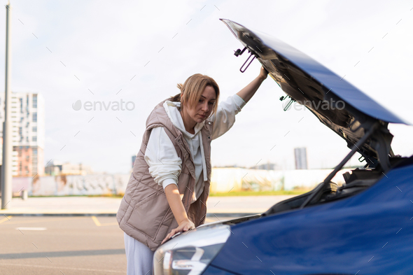 adult woman peeking under the hood of a car Stock Photo by traimakivan