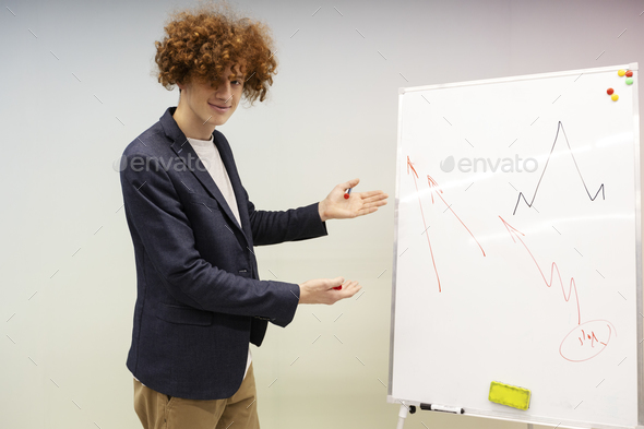 Smiling, attractive guy presenting graph drawn on flip chart. Young man ...