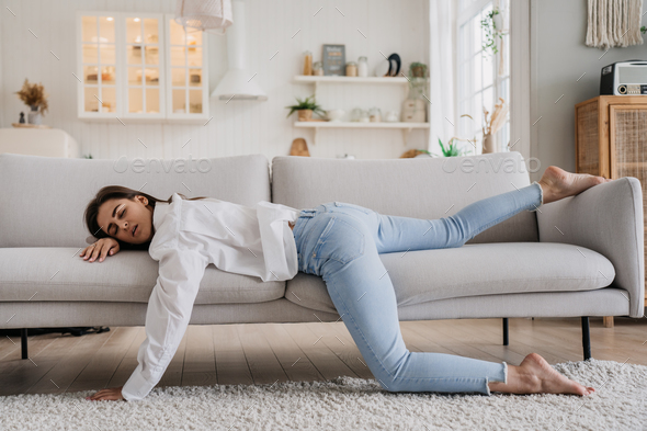 Tired woman in white shirt and jeans have sleeping on sofa. Tired female lying home alone at ...