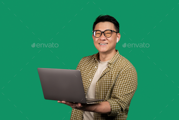 Positive asian man holding laptop computer and smiling at camera ...