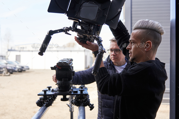 two caucasian men install a large professional camera on a camera ...