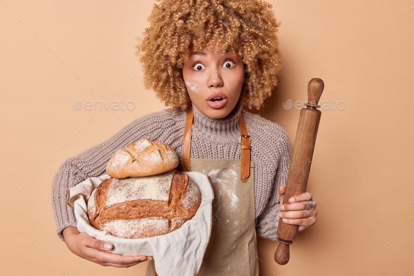 Scared female baker wears knitted jumper and apron holds two round ...