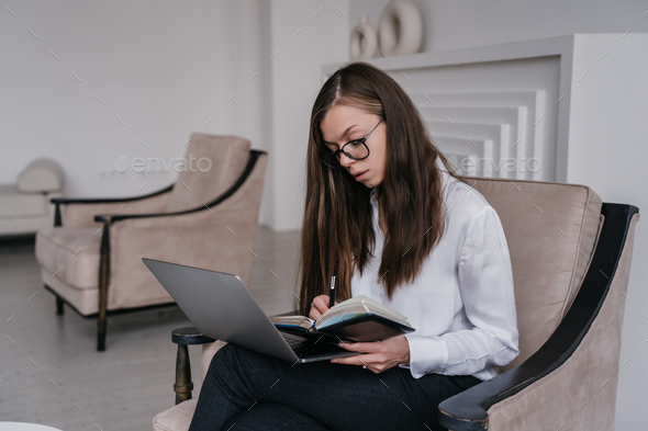 Overloaded brunette office manager sitting in chair using laptop holds ...