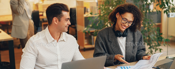 Two colleagues working together with documents while sitting on office ...