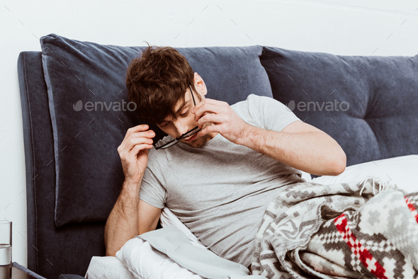 man waking up and putting on eyeglasses during morning time in bed at ...