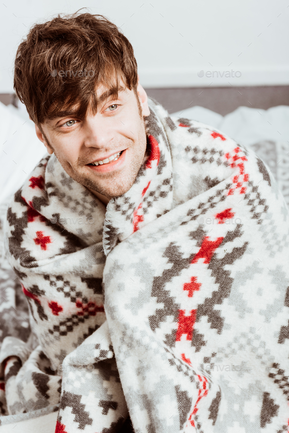 cheerful sick young man wrapped in blanket sitting on bed at home Stock ...