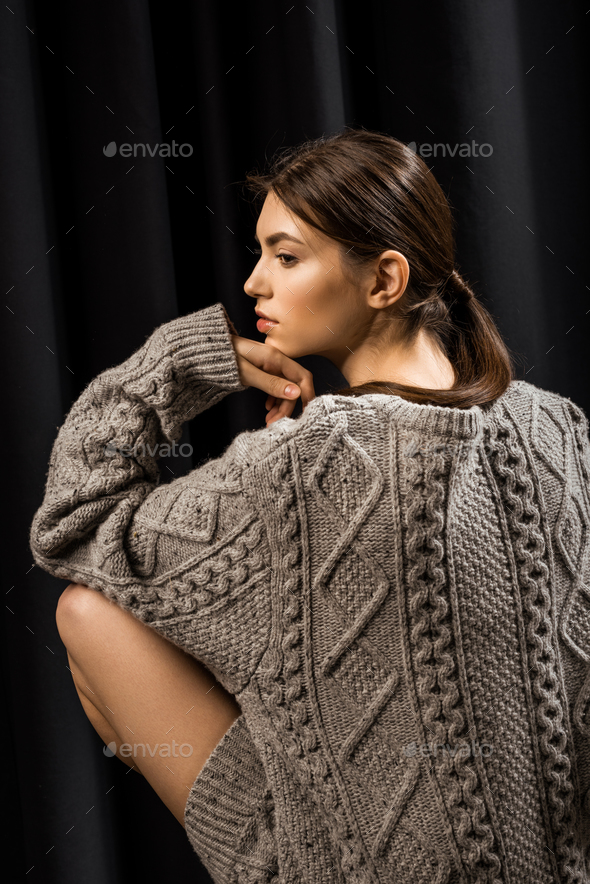 back view of beautiful young woman in woolen grey sweater on black ...