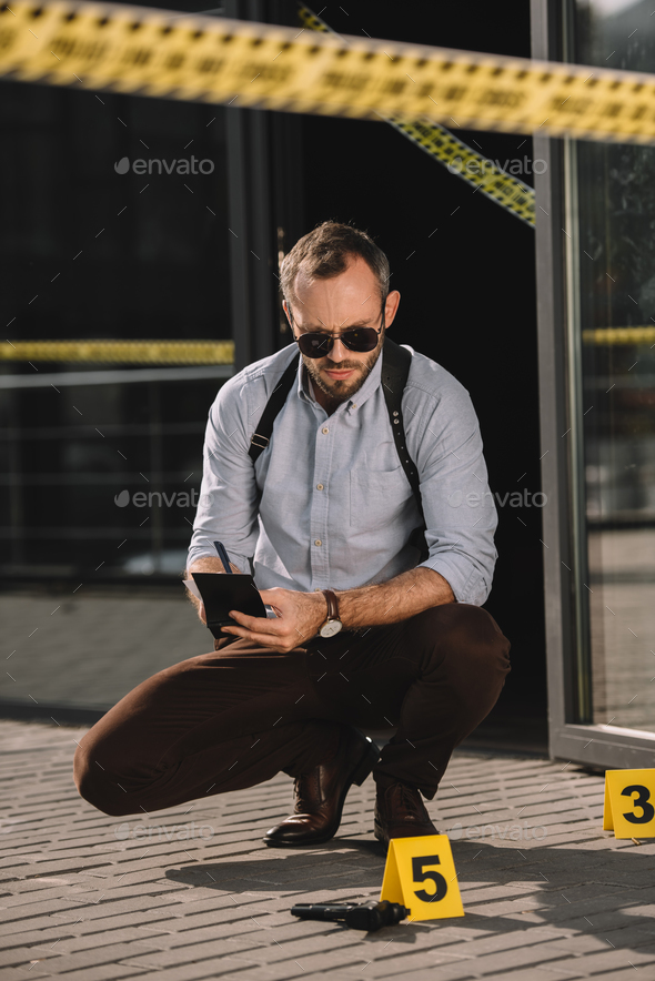 sitting male detective looking at the gun and make notes at crime scene ...