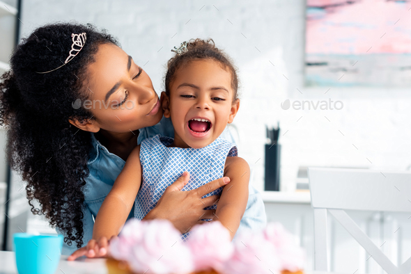 african american mother hugging excited daughter at table with cupcakes ...