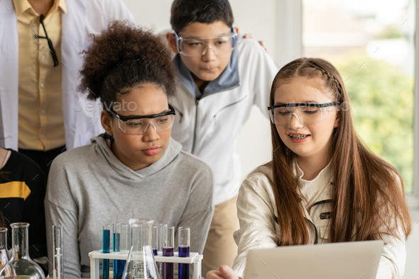Girl showing science experiment report on laptop to group of classmates ...