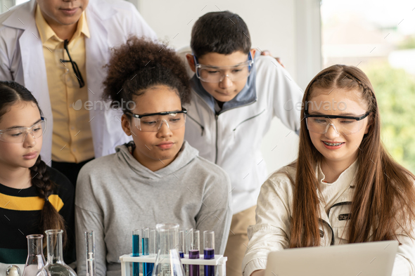 Girl showing science experiment report on laptop to group of classmates ...