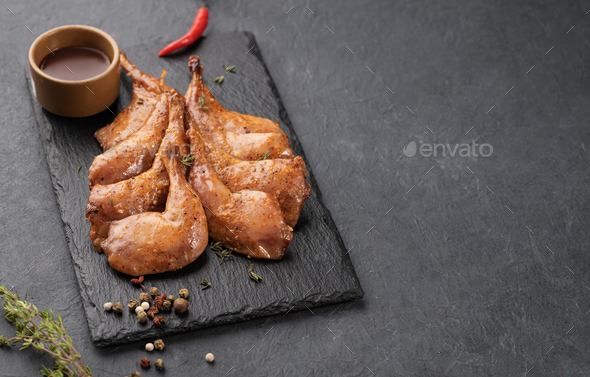 Delicacies. Grilled BBQ quail legs in marinade and spices on black ...