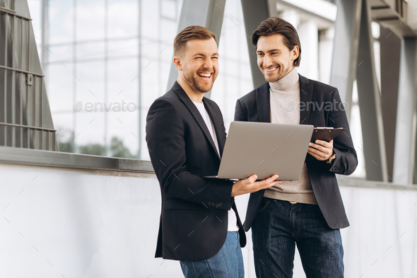 Two handsome young male businessmen in suits smiling hard and hold ...