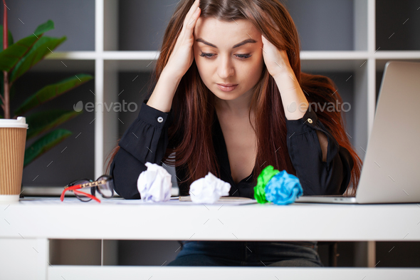 Sad business woman in office working on laptop Stock Photo by maksymiv