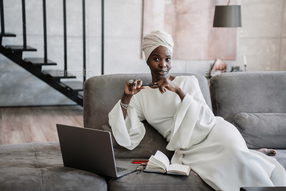 Curious African young woman in white dress and turban sits on cozy ...