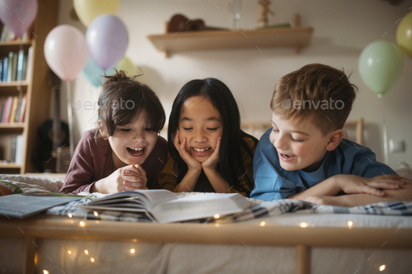Three happy friends reading a book together in a room. Stock Photo by ...