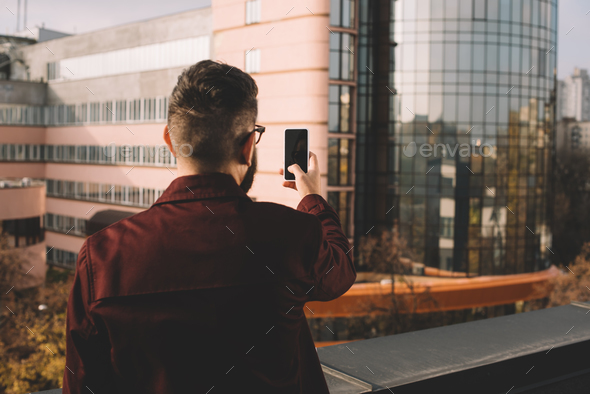 rear view of adult man taking selfie on rooftop with beautiful view ...