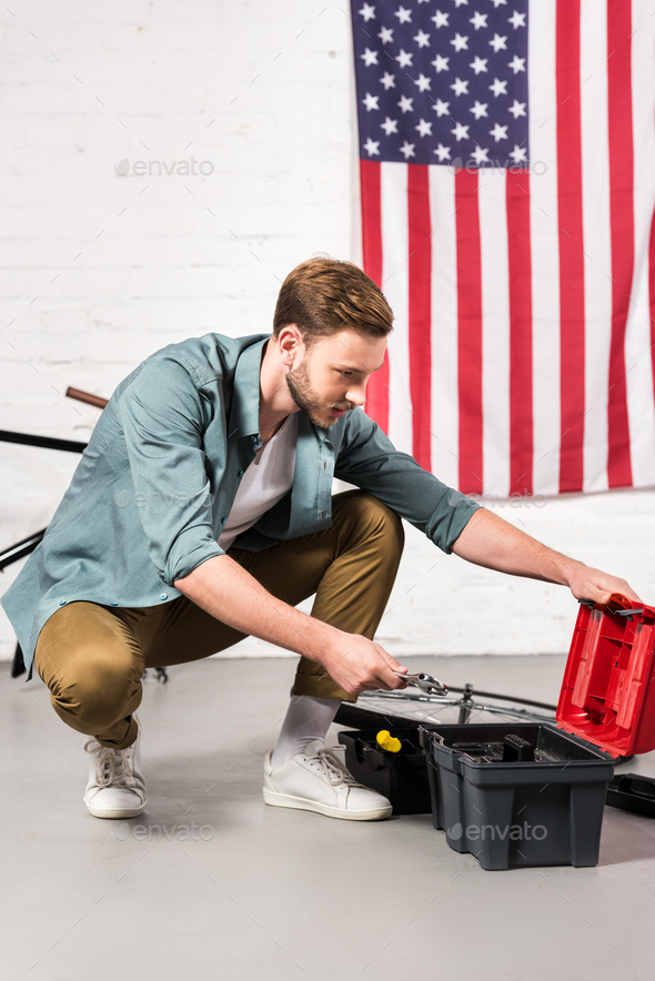 handsome young man putting adjustable wrench in tools box in front of ...