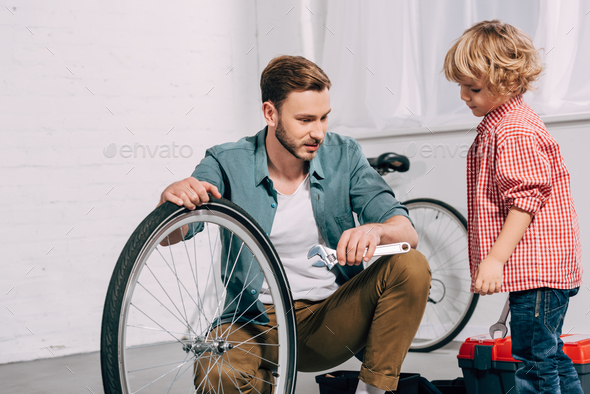 man with adjustable spanner sitting near bicycle wheel and talking to ...