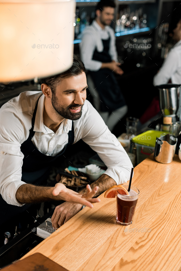 handsome smiling bartender serving cocktail with grapefruit slice and ...