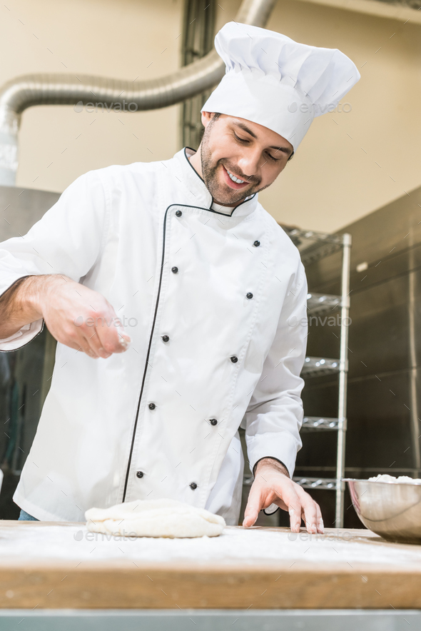 baker in white chefs uniform smiling and cooking dough in professional ...