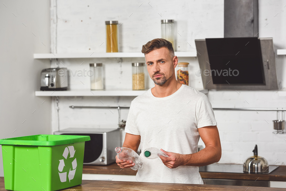 handsome man holding plastic bottles with green recycle box at wooden ...