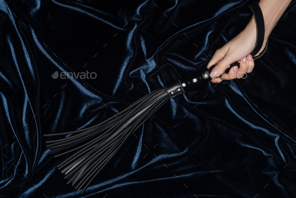 close up of of female hand holding flogging whip with dark velvet cloth ...