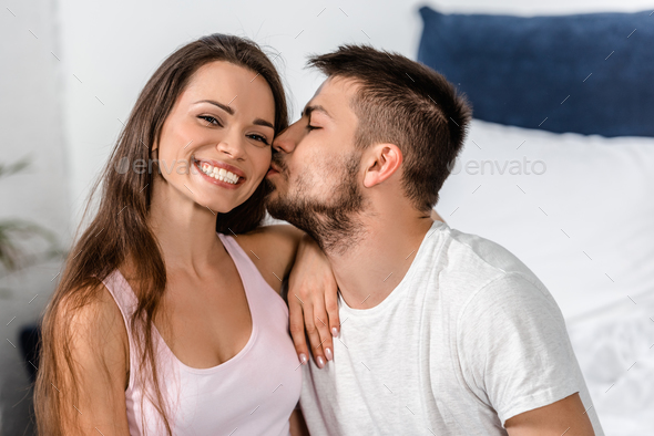 boyfriend in pajamas hugging and kissing smiling girlfriend on bed in ...