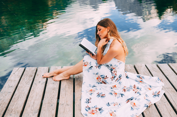 Attractive young woman reading book on dock next to the lake Stock ...