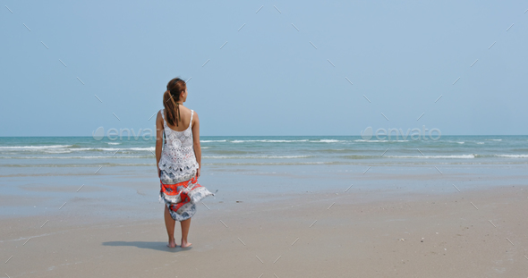 Woman walk on beach and look at the sea Stock Photo by leungchopan