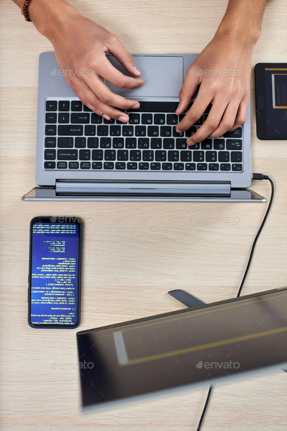 Male hands typing and writing code for mobile devices at light wood ...