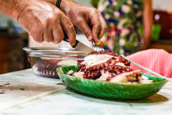 Male hands cutting with a knife a octopus leg in the kitchen, plate ...