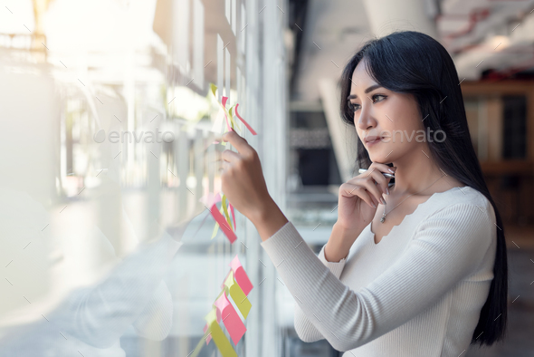 Close up hand businesswoman writing sticky notes on glass wall in ...