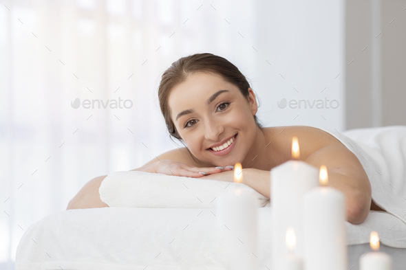 Beautiful woman lying on massage table in spa next to burning candles ...