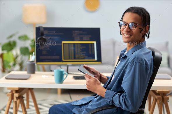 Smiling computer programmer holding tablet and writing code at ...