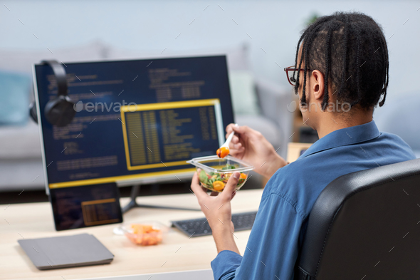Young computer programmer eating takeout lunch at workplace while ...