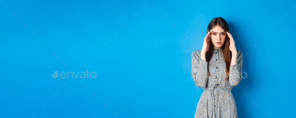 Woman trying to concentrate, touching head and squinting at camera ...