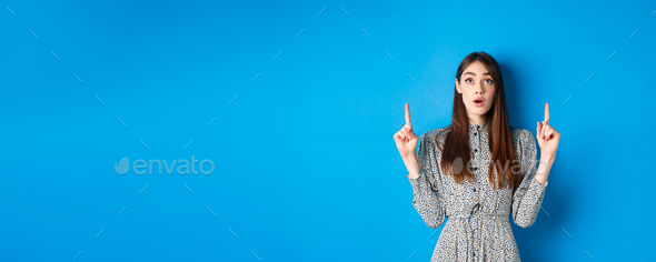 Surprised romantic girl in dress pointing, looking up with opened mouth ...