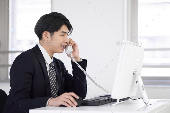 A Japanese male businessman answering the phone with a smile on his ...