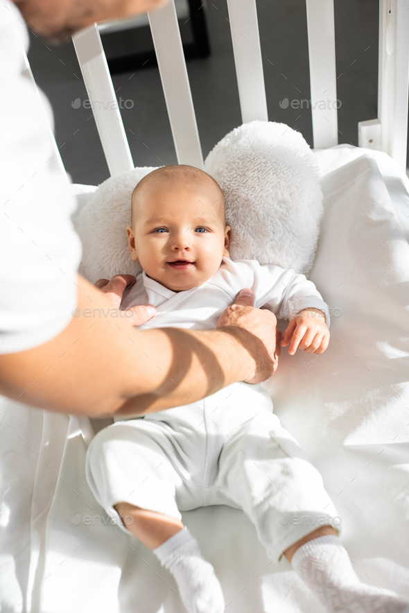 cropped view of father putting cheerful baby into baby crib Stock Photo ...