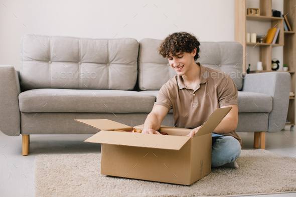 Happy young smiling curly man opening box with ordered goods gifts ...