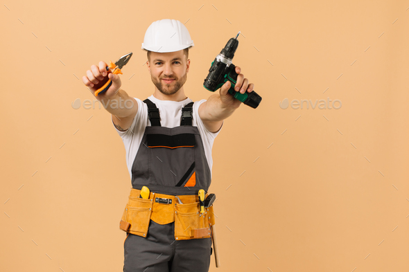 Positive male repairman at home shows screwdriver and pliers on beige ...