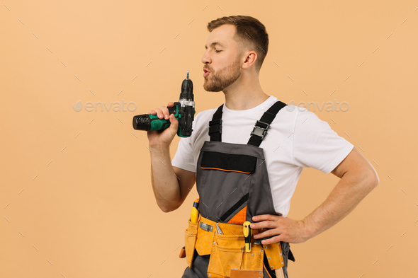 Positive male repairman at home with screwdriver on beige background ...