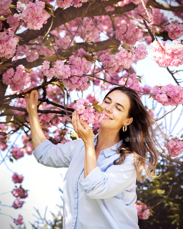 Beautiful smiling woman on the background of lilac pink cherry blossoms ...