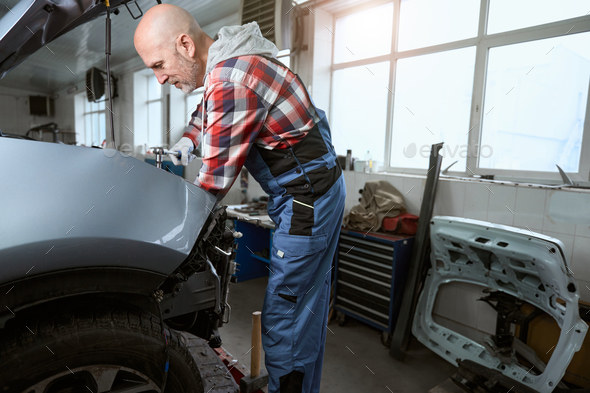 Auto repairman at the workplace repairs a car Stock Photo by Iakobchuk