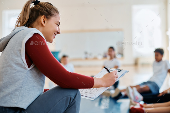 Happy sports teacher taking notes during PE class at school gymnasium ...